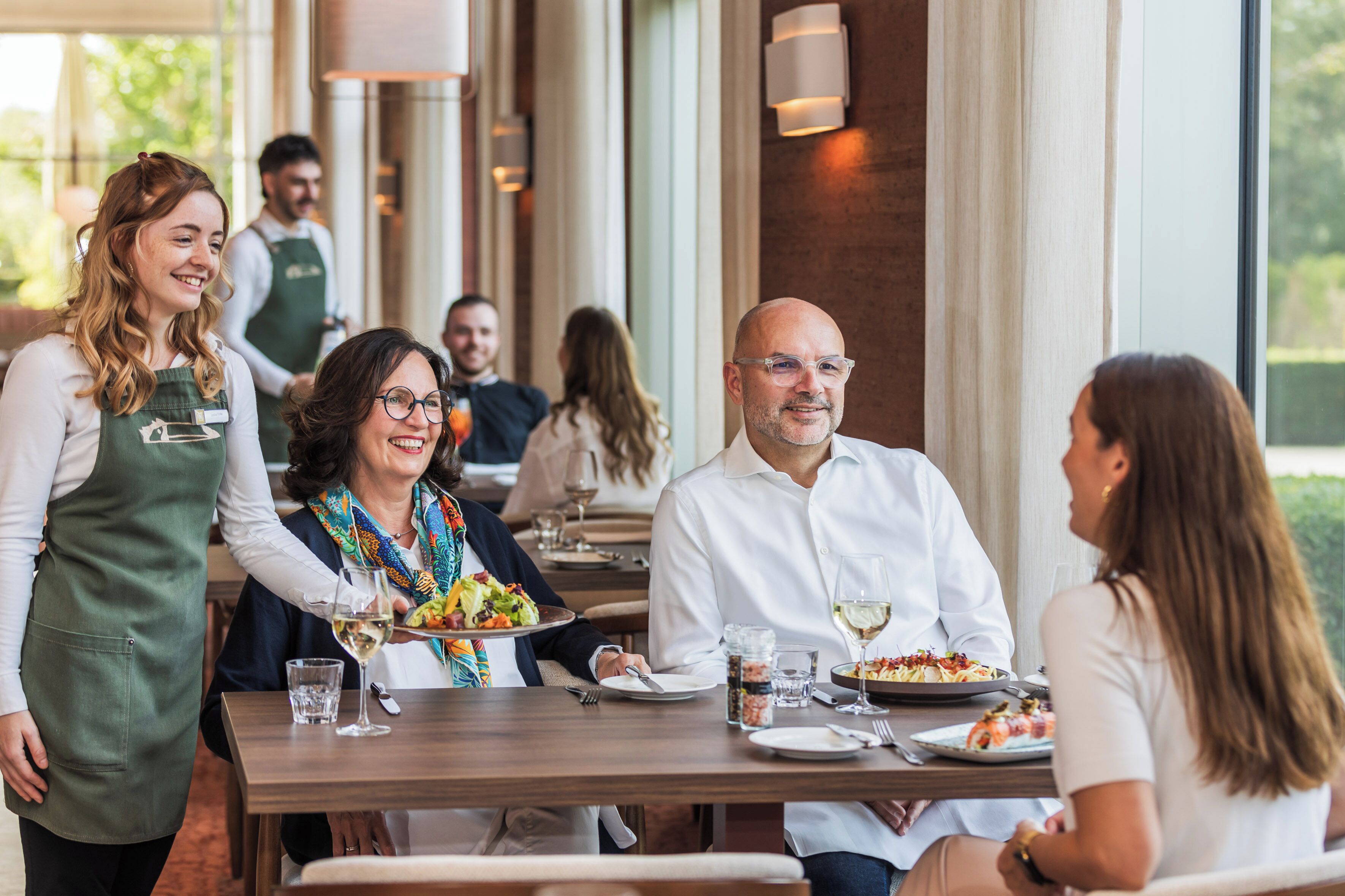 Interior de restaurante com um garçom servindo um prato a uma mesa.