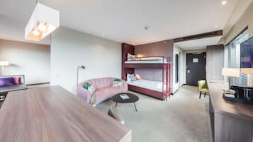 Quarto de hotel moderno com beliche, sofá, mesa de jantar e escrivaninha.