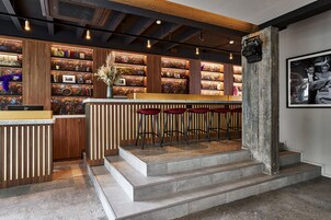 Uma área de bar moderna com prateleiras de madeira, banquetas vermelhas e uma escadaria de concreto.