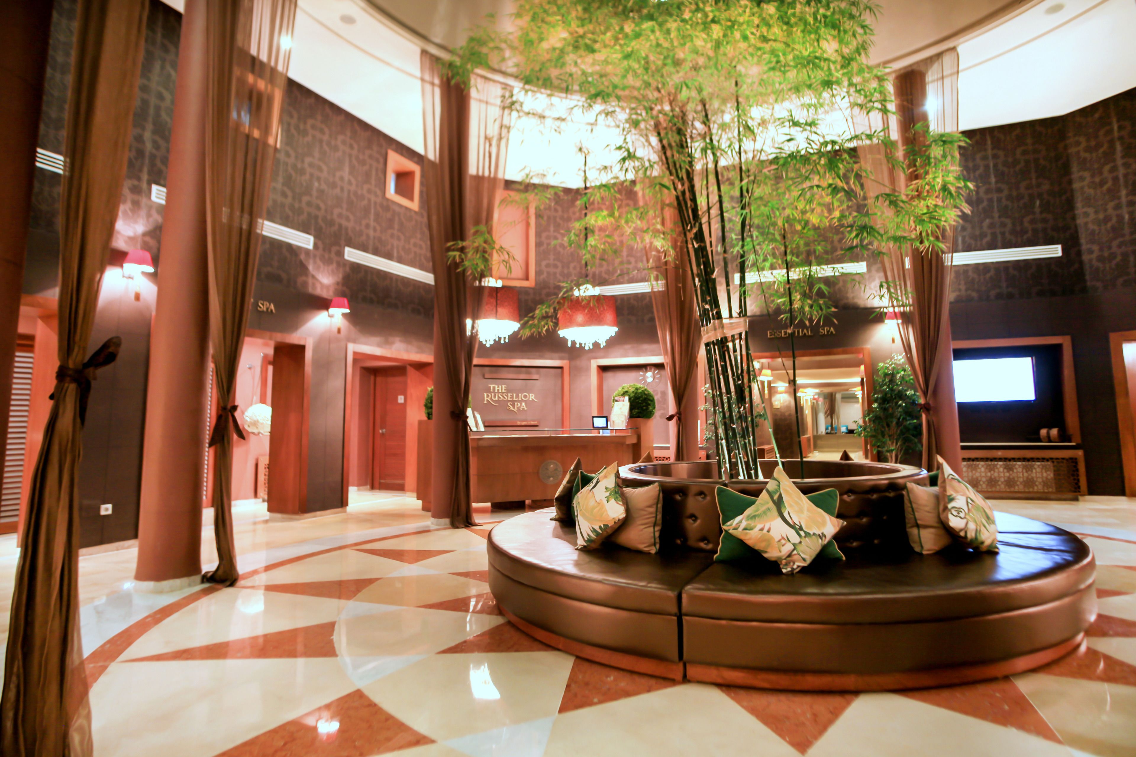 Um lobby com área de estar central, balcão de recepção e uma grande planta.