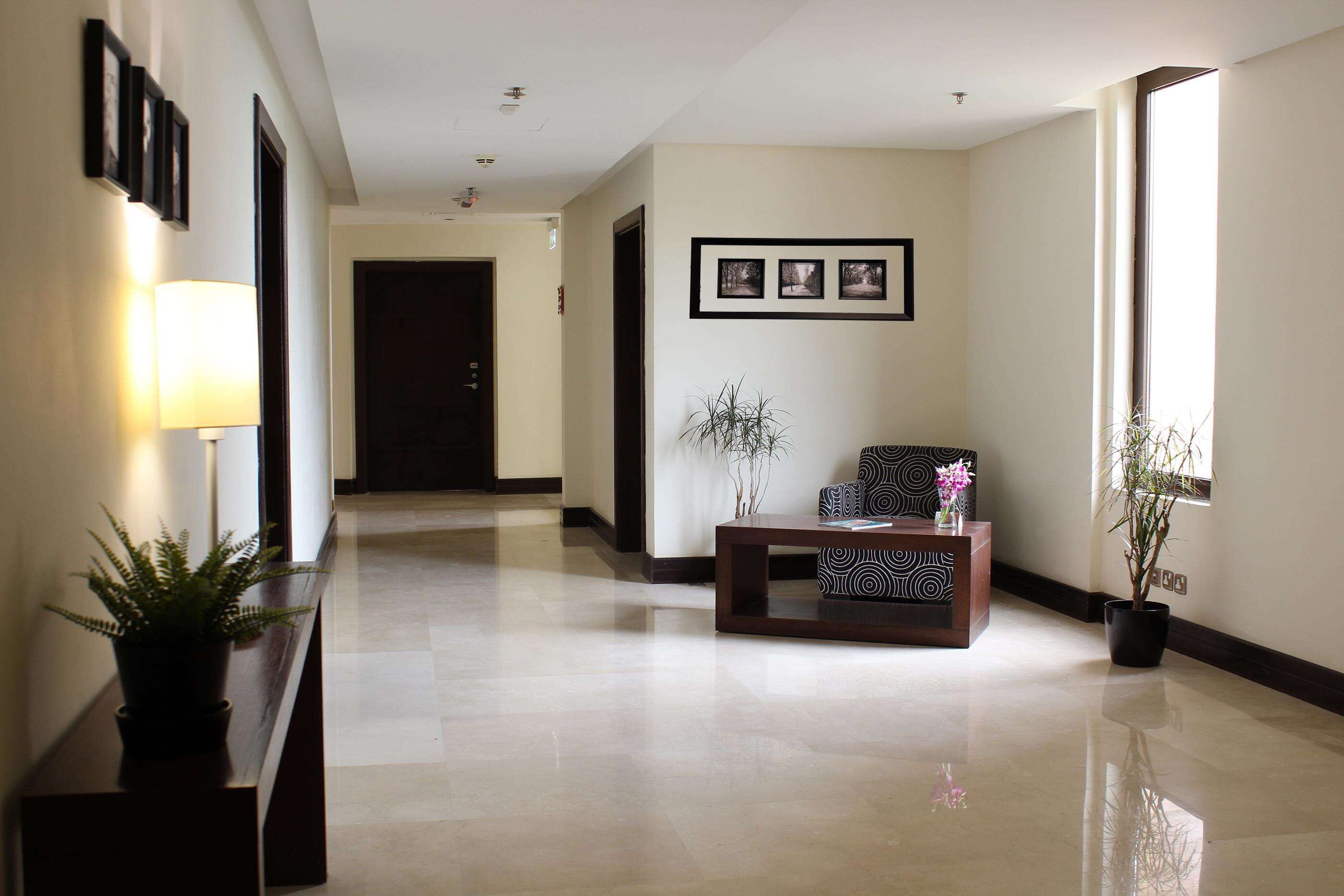 Um corredor com balcão de recepção, quadros nas paredes e plantas em vasos.