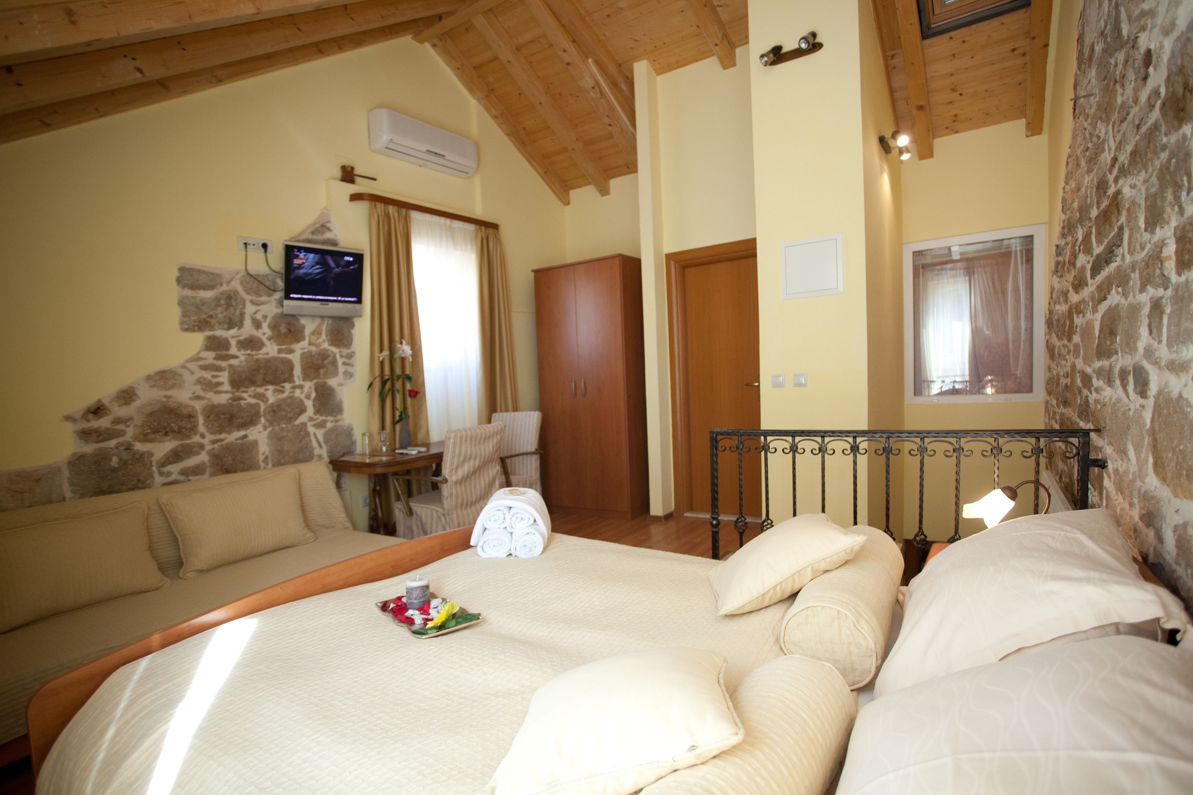 Quarto com parede de pedra, vigas de madeira no teto, cama com almofadas, televisão na parede e lareira de pedra.
