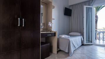 Quarto de hotel com um guarda-roupa de madeira escura, uma pequena secretária com espelho, uma cama com colcha branca e uma varanda com vista.