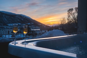 Duas taças de vinho em uma varanda com vista para uma paisagem nevada ao pôr do sol.