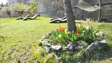 Um jardim com uma rede, cadeiras reclináveis e diversas plantas, incluindo tulipas.