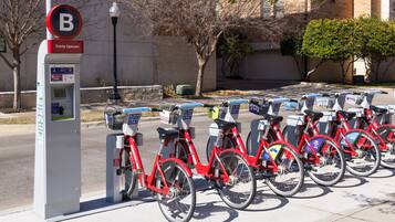 Uma fileira de bicicletas vermelhas estacionadas em uma estação de compartilhamento de bicicletas, com uma placa indicando Trinity Uptown.
