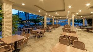 Uma área externa de café com várias mesas e cadeiras, uma mesa de bilhar e vista para os edifícios ao redor.