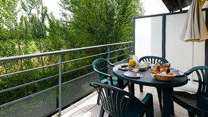 Varanda com mesa posta para o café da manhã, cadeiras e vista para o verde.