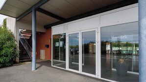 Um edifício com entrada coberta, portas de vidro e escadaria para um andar superior.