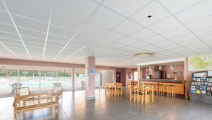 Um hall amplo com vista para a piscina, mobiliário de madeira e um balcão de recepção.