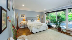 Quarto com cama, duas luminárias de cabeceira, uma cadeira, uma janela grande e um vaso com planta.
