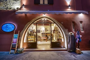 Entrada de um hotel boutique com uma porta em arco característica, um letreiro de neon e diversos objetos expostos no interior.