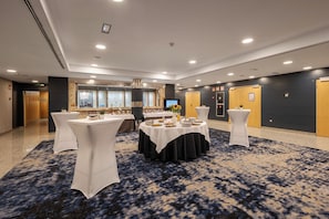 Sala de conferências com mesas redondas, uma tela grande e um balcão de recepção.