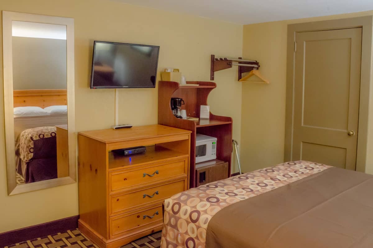 Quarto de hotel com cama, televisão, cómoda de madeira, micro-ondas e uma porta.