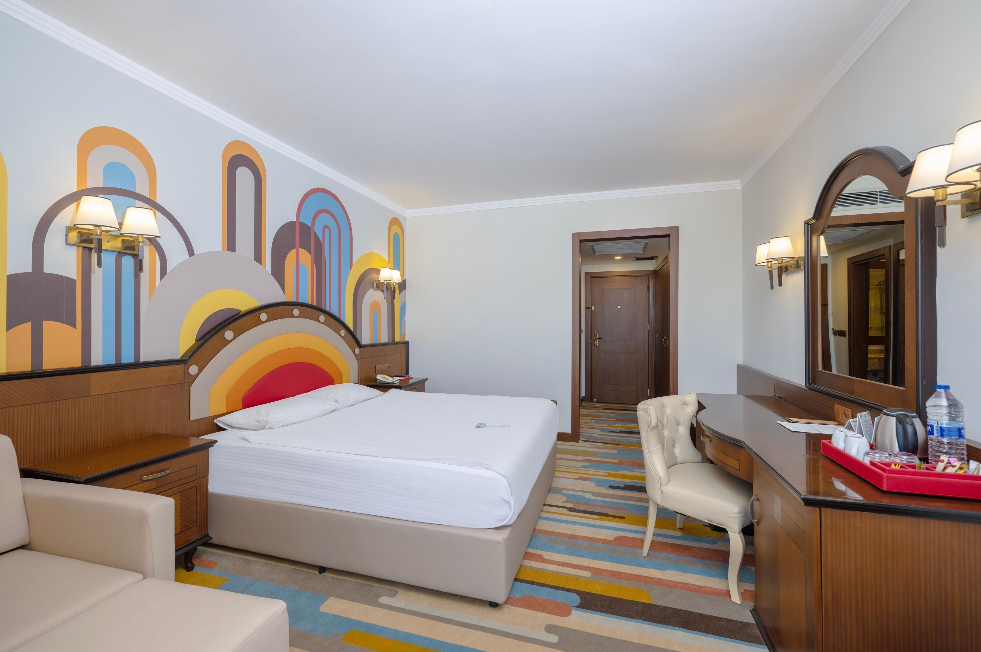 Quarto de hotel com cama, escrivaninha, cadeira, cômoda e porta do banheiro.