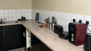Uma cozinha com bancada de madeira clara, armários pretos, torradeira e cafeteira.