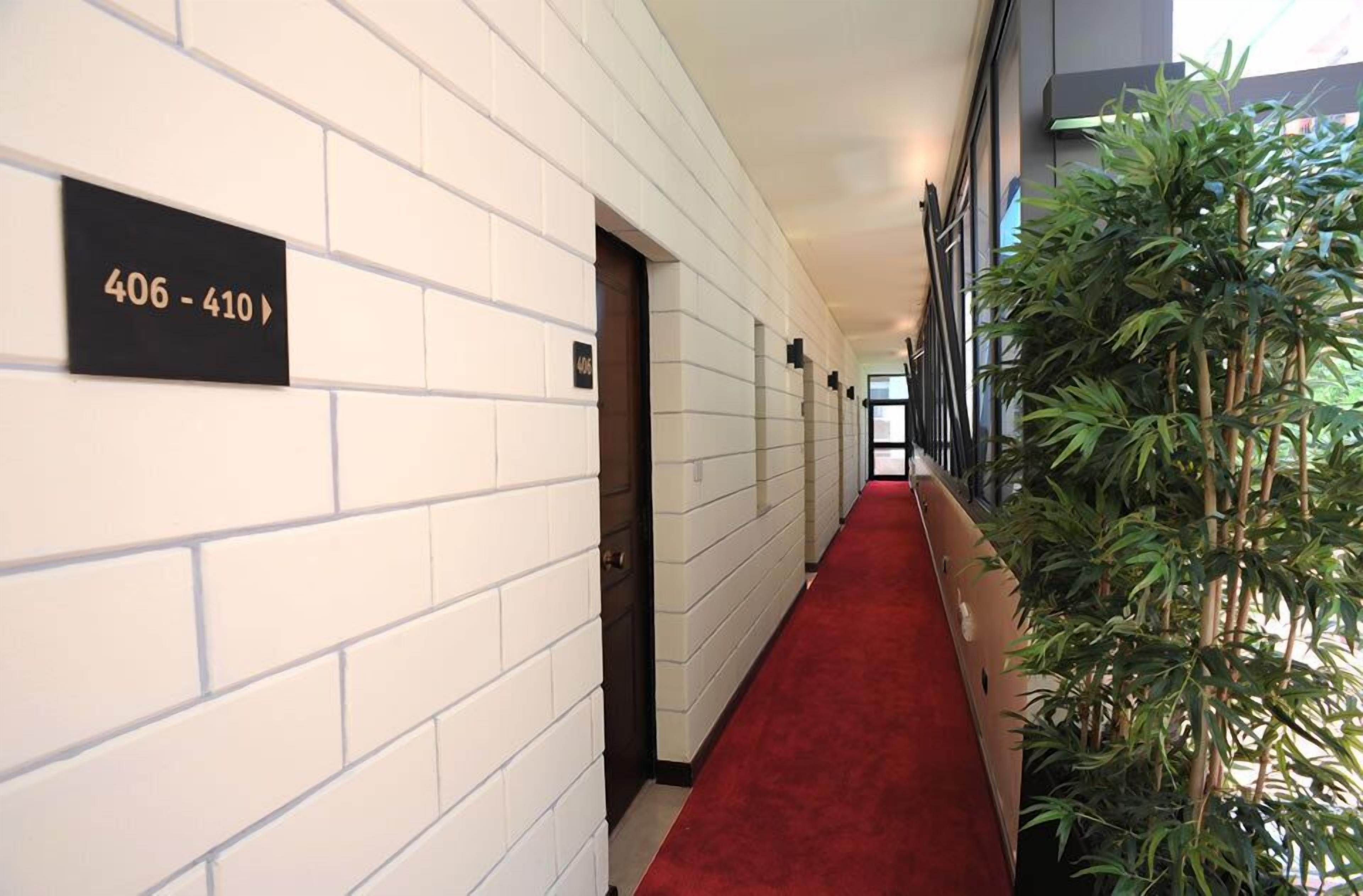 Um corredor com paredes de tijolos brancos, tapete vermelho e uma placa indicando os números dos quartos 406 a 410.