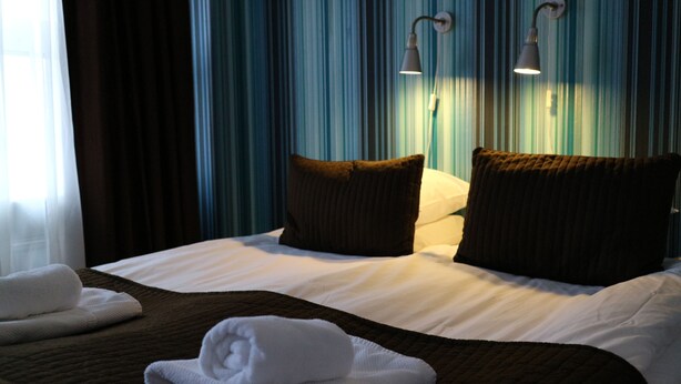 Quarto de hotel com uma cama, duas almofadas, um cobertor e uma toalha dobrada.