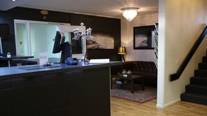 Uma sala de estar moderna com um balcão de recepção em tons escuros, um lustre, um sofá e uma escada.