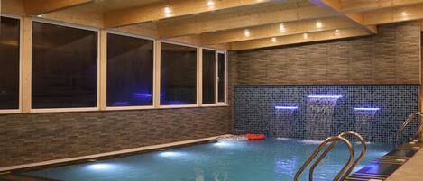 Piscina interior com faixas de natação bem definidas, parede revestida com elementos aquáticos e teto de madeira.