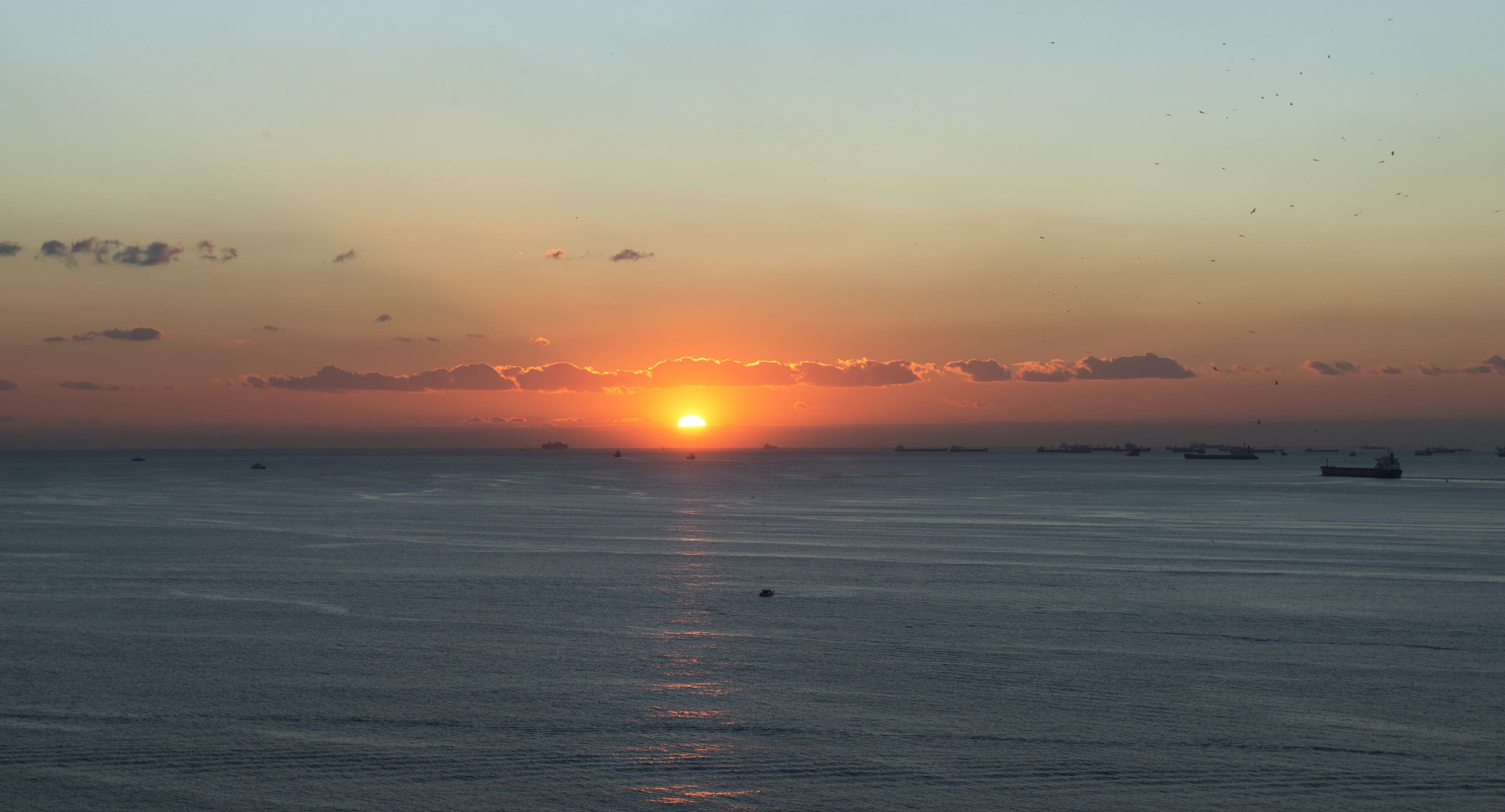 Um pôr do sol sobre um mar calmo, com vários navios ao longe.