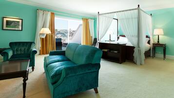 Quarto de hotel com sofá verde-água, cama com dossel, escrivaninha e uma cadeira.