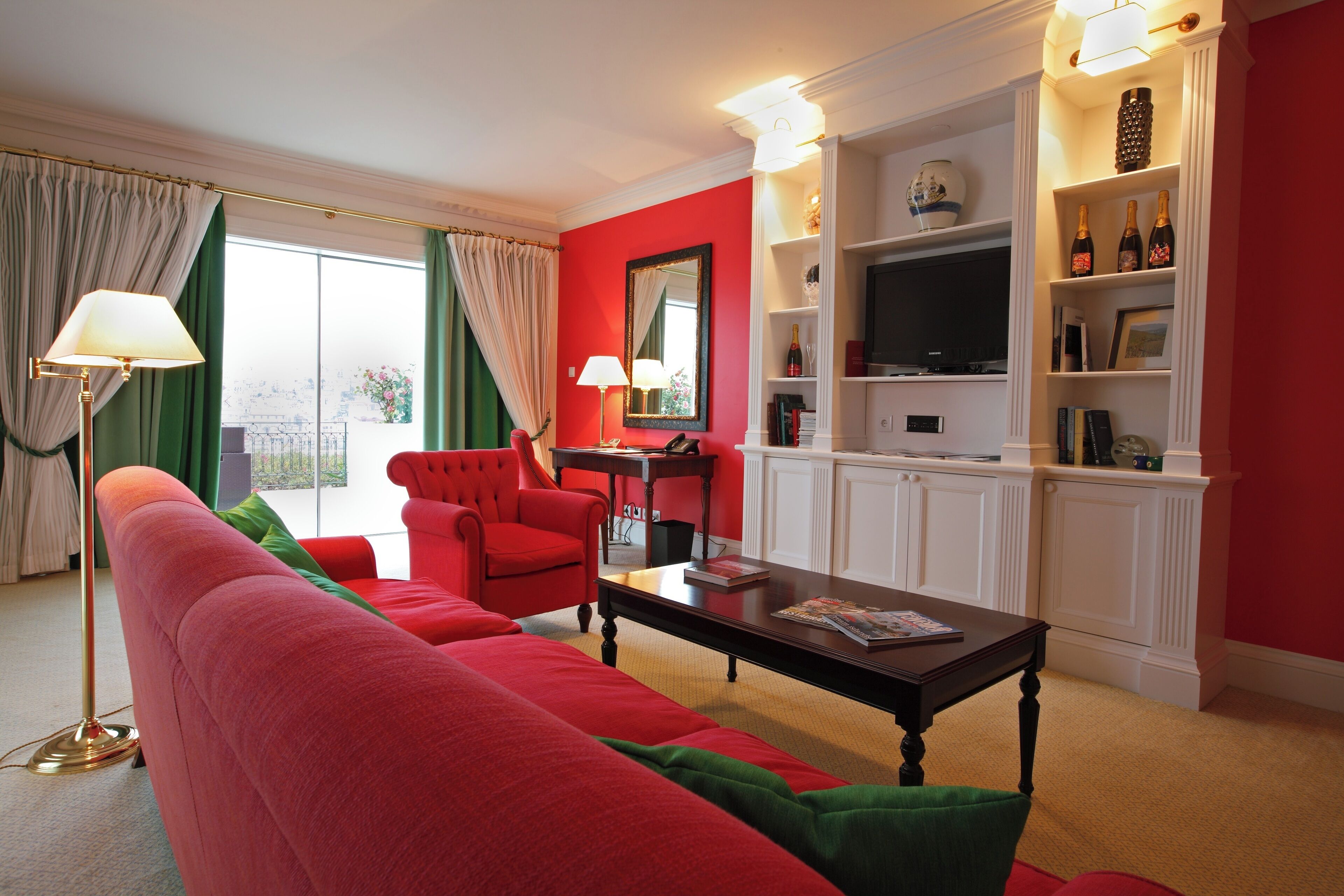 Uma sala de estar com um sofá vermelho, almofadas verdes, uma poltrona vermelha, uma mesa de centro e uma estante para TV.