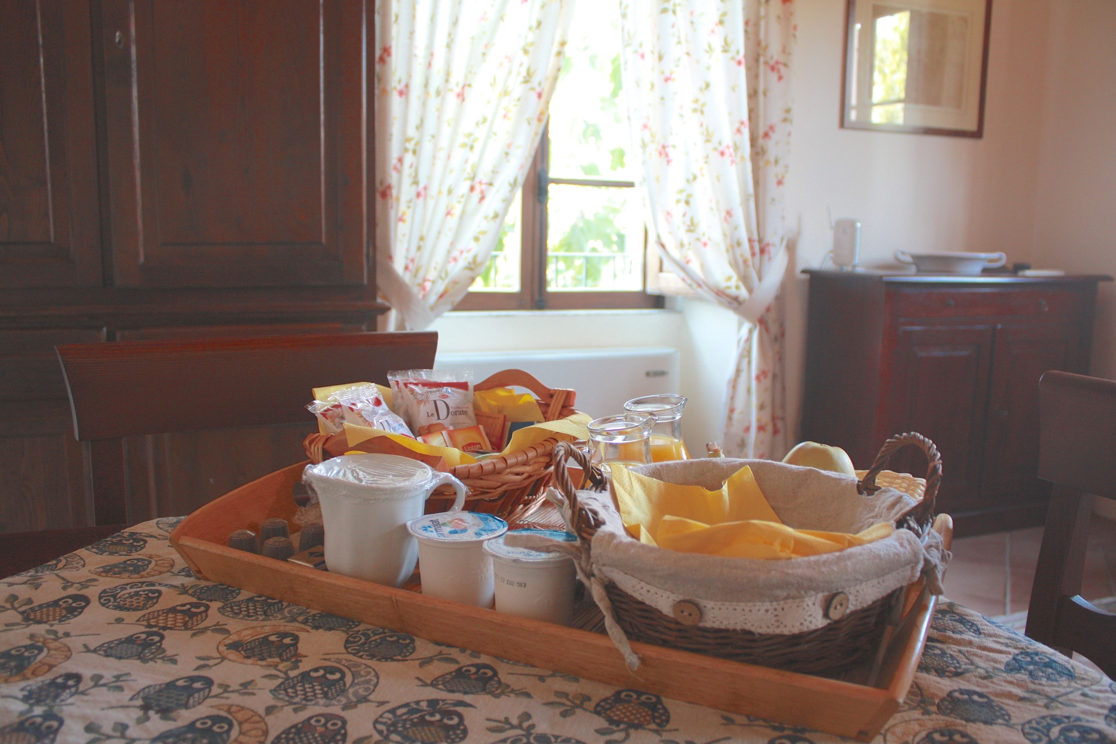 Bandeja de café da manhã com diversos alimentos e recipientes sobre uma mesa com toalha de mesa estampada.