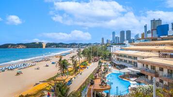 Paisagem costeira com praia, piscina e edifícios altos.