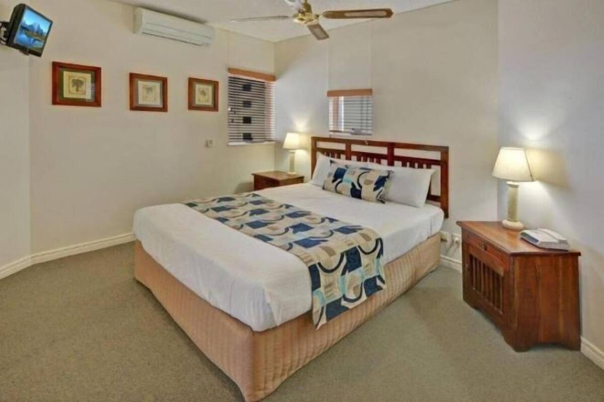 Quarto com cama, abajures, televisão e quadros nas paredes.