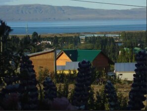 Paisagem rural com um pequeno conjunto de construções, um corpo d'água e montanhas ao fundo.