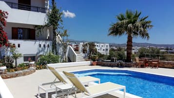 Área de piscina com espreguiçadeiras, um muro de pedra e vista para edifícios e montanhas ao fundo.