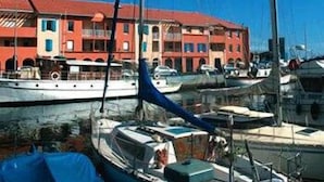 Uma marina com barcos atracados, um edifício vermelho com várias varandas e um céu azul e claro.