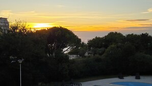 Piscina com espreguiçadeiras, cercada por árvores e vista para o pôr do sol.