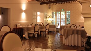 Uma sala de jantar com várias mesas, cadeiras e teto com vigas aparentes.
