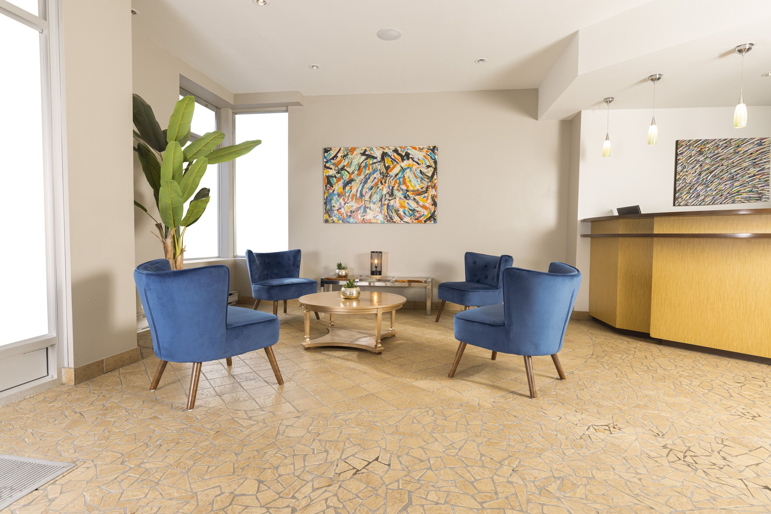 Um hall de entrada com uma mesa de recepção, duas poltronas azuis, uma mesa de centro e uma grande pintura abstrata na parede.