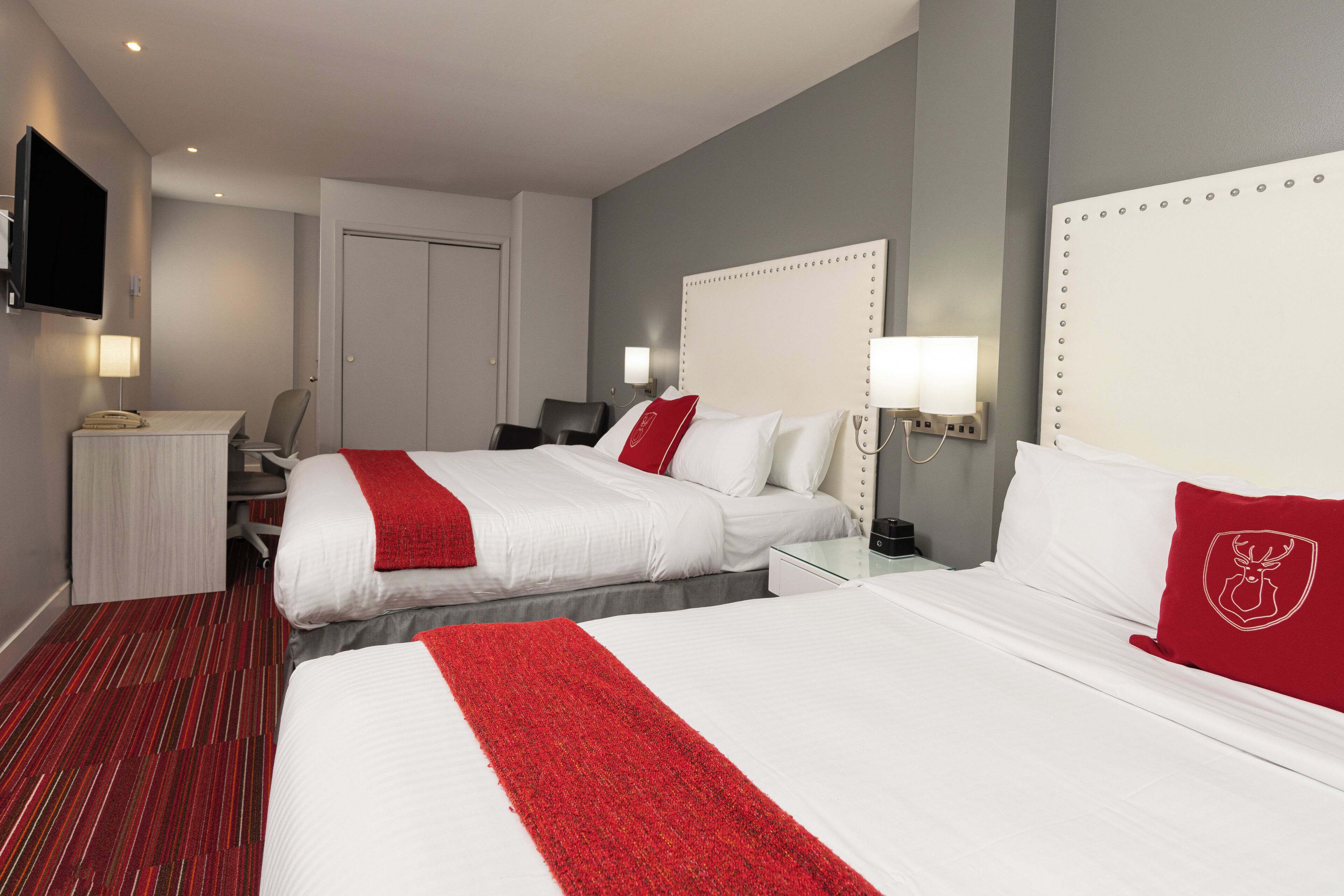 Quarto de hotel com duas camas, uma mesa, uma cadeira, uma televisão e uma porta.