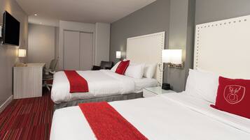 Quarto de hotel com duas camas, uma mesa, uma cadeira, uma televisão e uma porta.