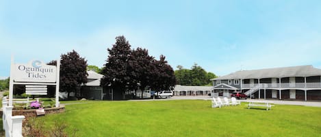 Uma área gramada com uma placa para Ogunquit Tides Resort Property, um edifício com varanda coberta e um cercado branco.