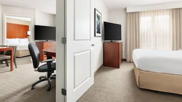 Quarto de hotel com cama, escrivaninha, cadeira, televisão e porta.