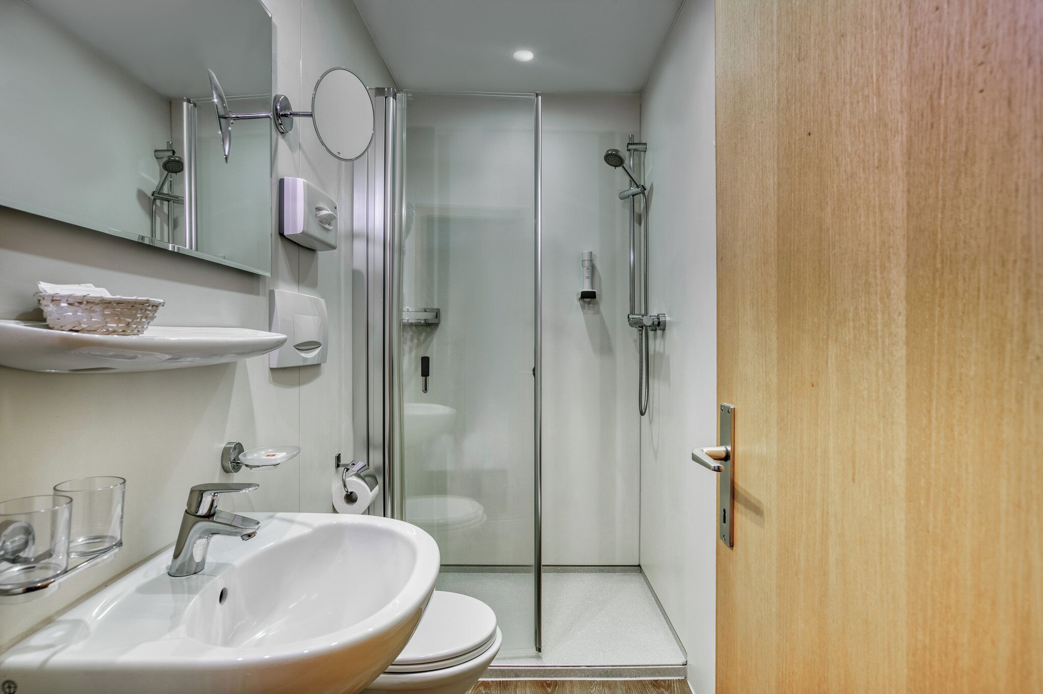 Uma casa de banho moderna com chuveiro em cabine de vidro, lavatório branco e sanita.