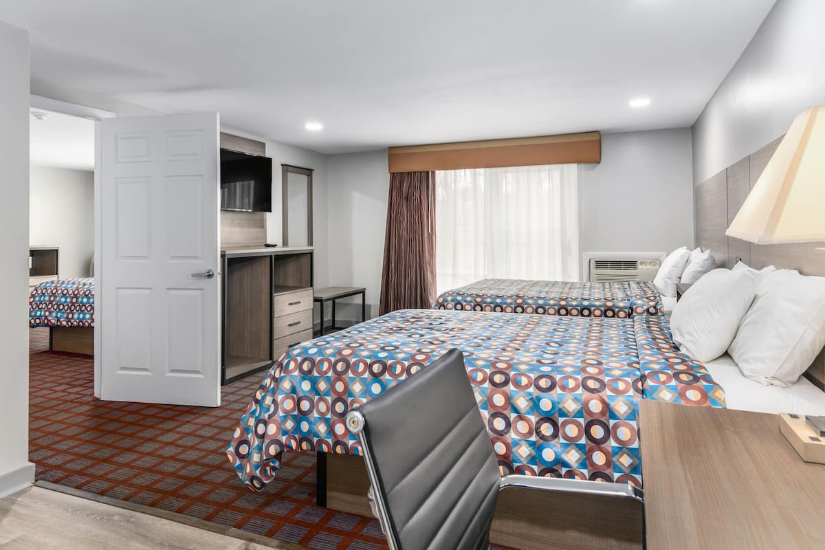 Quarto de hotel com duas camas, uma escrivaninha, uma cadeira, um guarda-roupa e uma janela com cortinas.