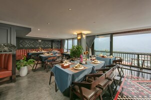 Restaurante com mesas preparadas para refeições, varanda com vista e parede com padrão.