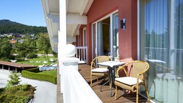 Varanda com cadeiras de vime e uma mesa, com vista para uma piscina e área arborizada.