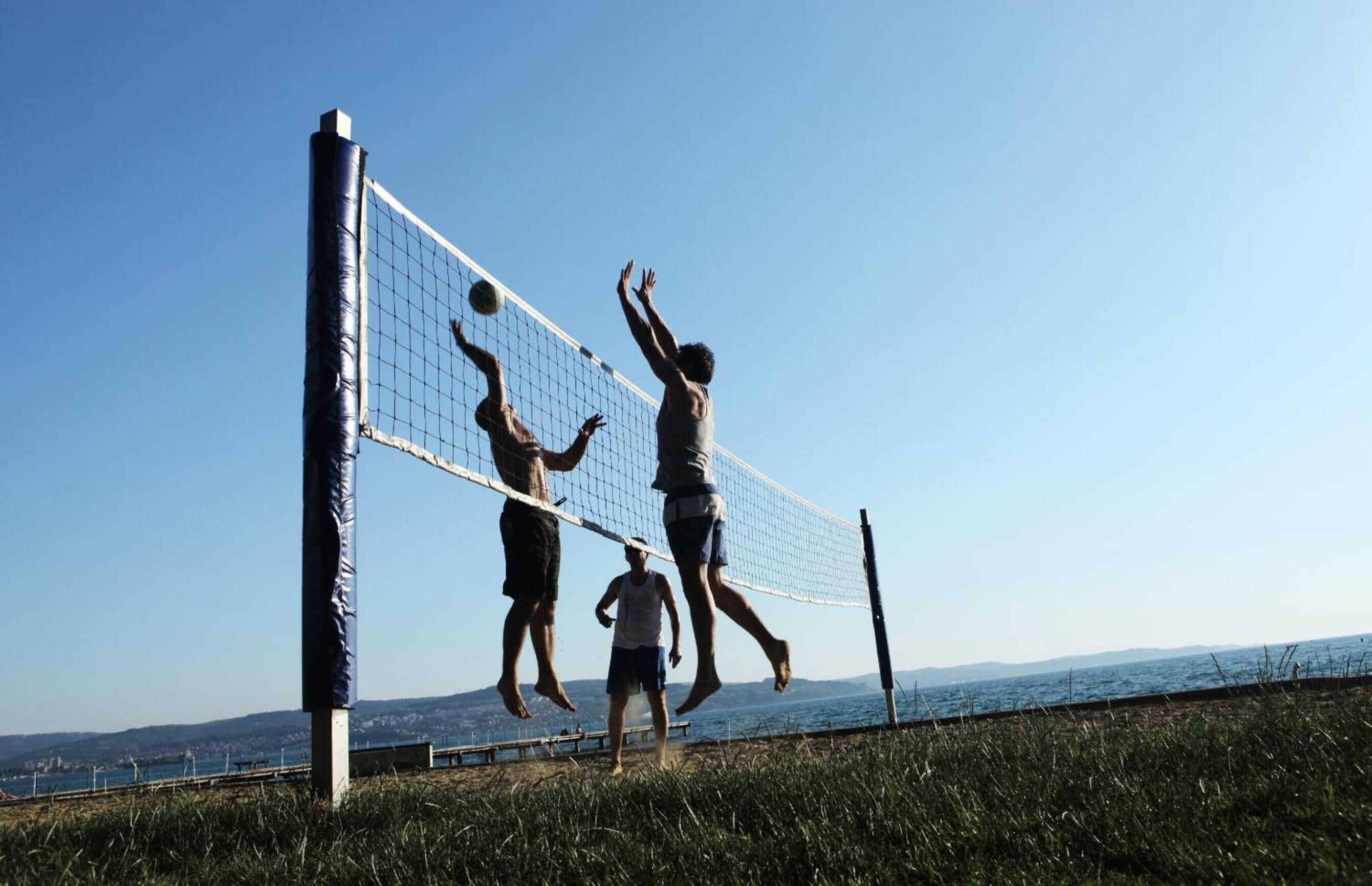 Jogo de voleibol de praia com jogadores a saltar sobre a rede.