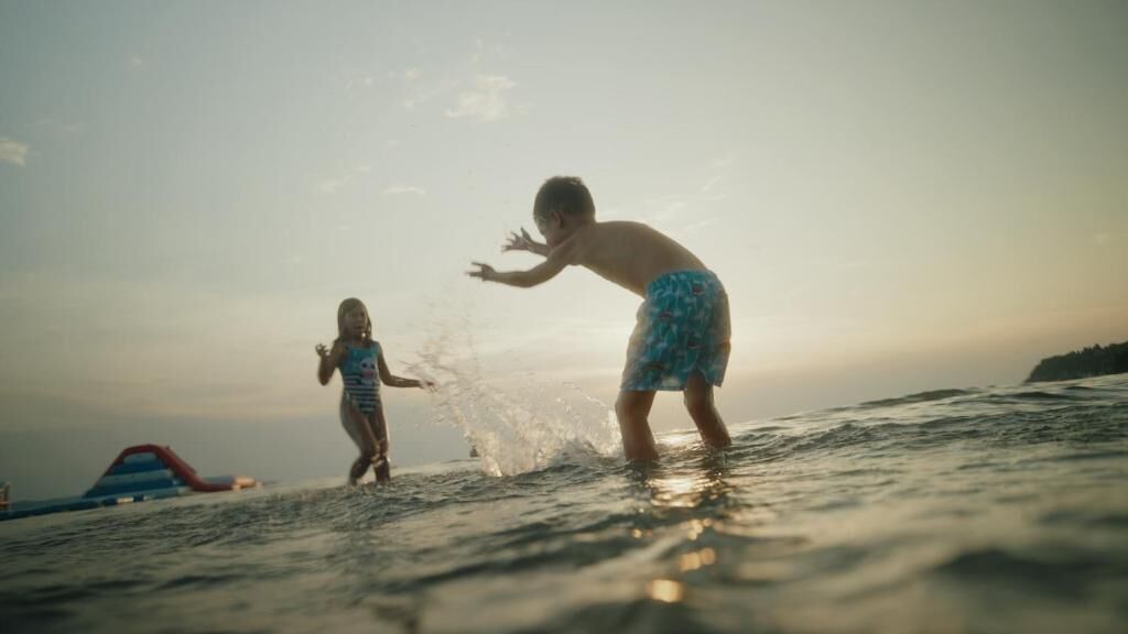 Duas crianças brincando na água na praia durante o pôr do sol.