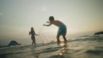 Duas crianças brincando na água na praia durante o pôr do sol.