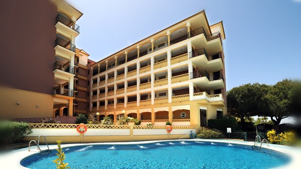 Um hotel com vários andares, piscina, varandas e área ajardinada com plantas.