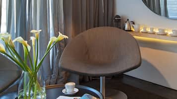 Quarto de hotel moderno com uma mesa redonda, uma poltrona confortável, um vaso com flores, uma xícara de café e uma revista.