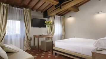 Quarto de hotel com cama, escrivaninha, cadeira, televisão e cortinas.